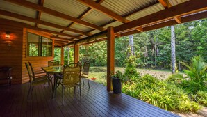 Um deck de madeira com mesa e cadeiras, cercado por vegetação exuberante e vista para a floresta.