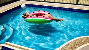 Uma pessoa flutuando em um piscinão em um brinquedo inflável rosa e verde.