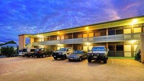 Hotel com estacionamento, vários veículos e varanda.