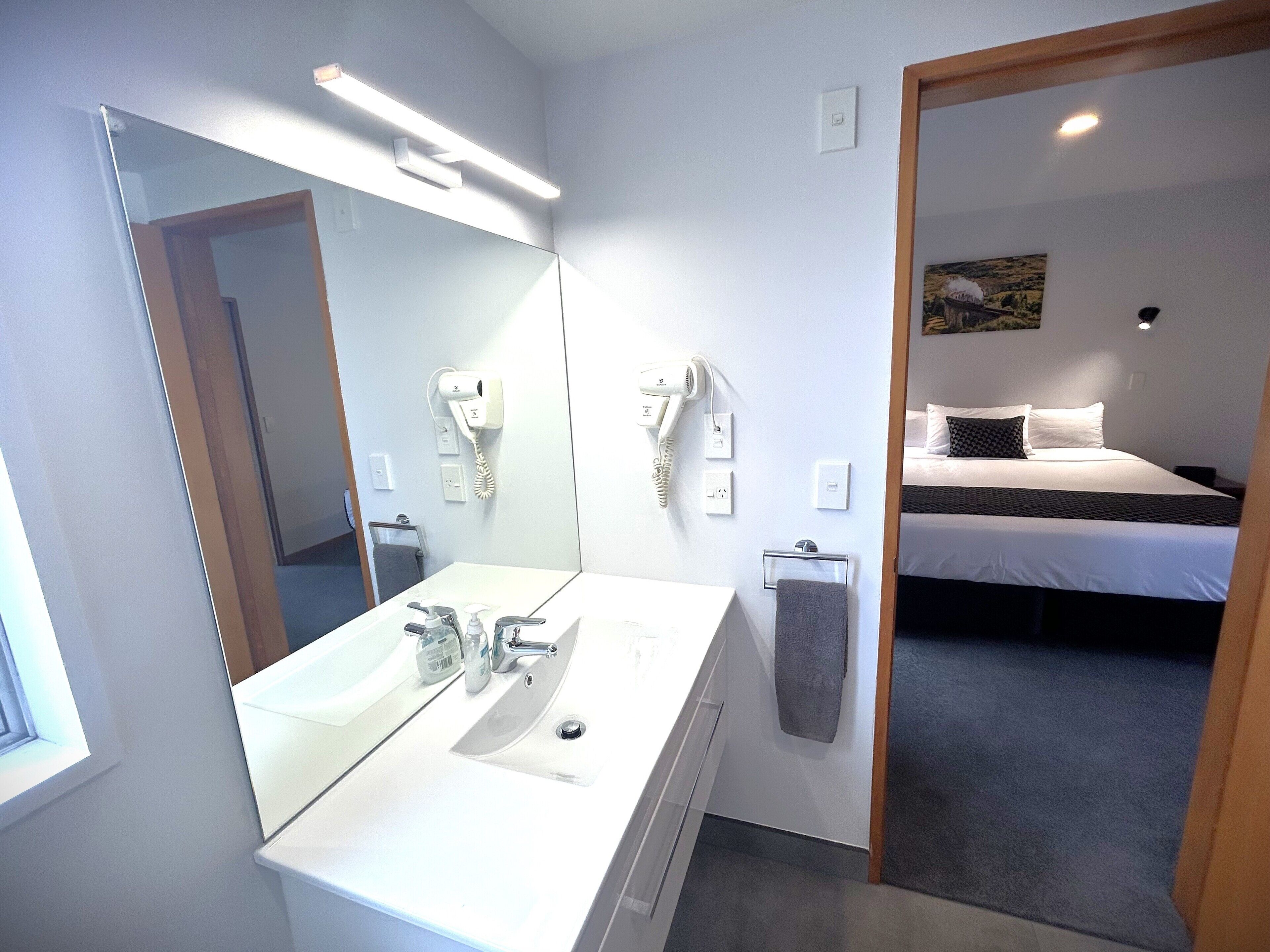 Casa de banho de hotel com um espelho grande, uma pia, um secador de cabelo e um porta-toalhas.