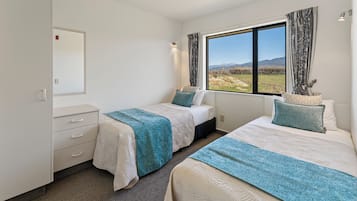 Quarto de hotel com duas camas, uma cômoda e uma janela ampla com vista para montanhas.