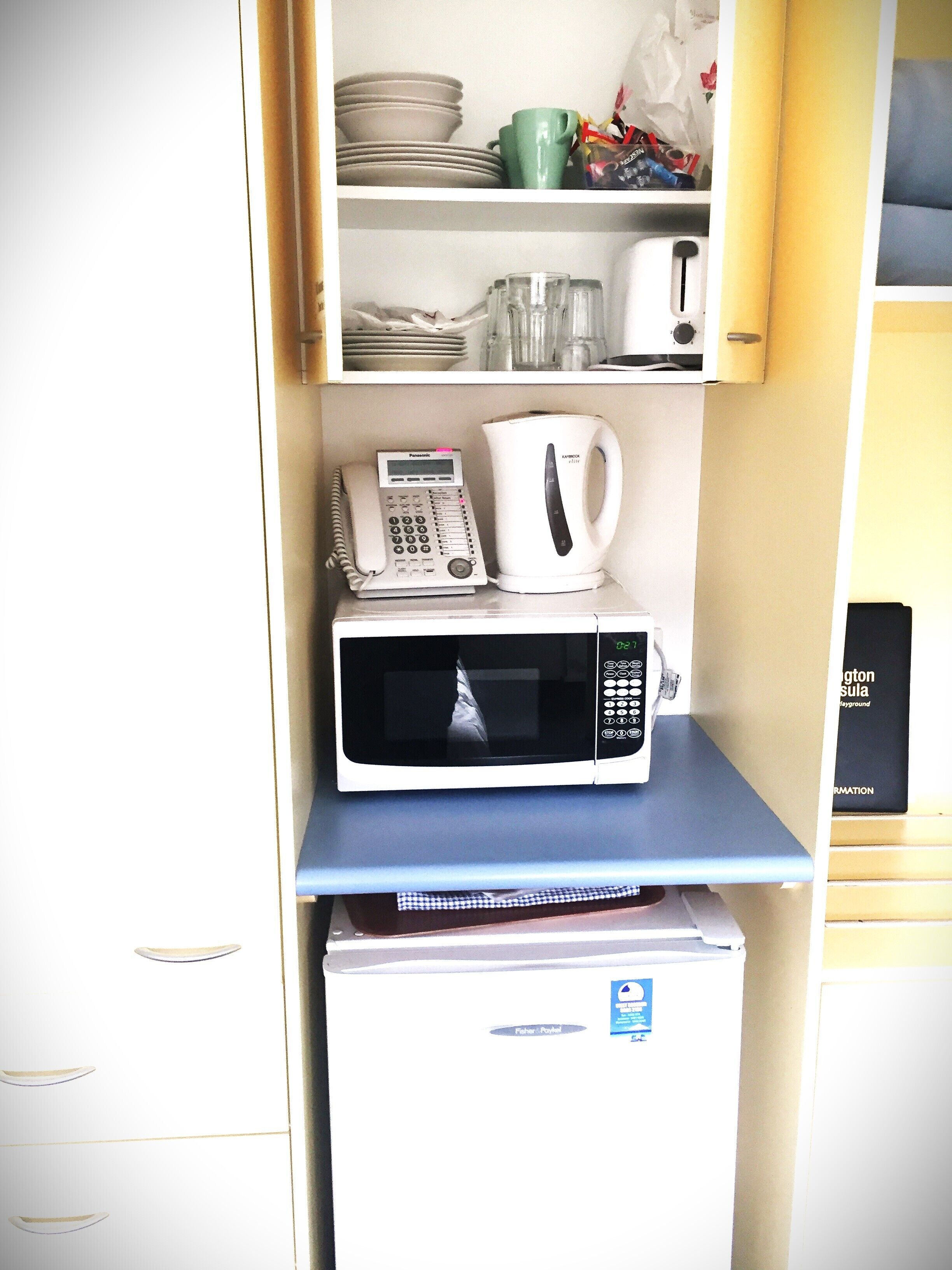 Uma cozinha compacta equipada com micro-ondas, máquina de café e telefone.