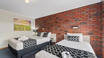 Quarto de hotel com duas camas, parede de tijolos e pintura de um vinhedo.