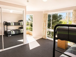 Quarto com beliche, uma cama de solteiro, mesa de cabeceira de madeira e uma janela grande com cortinas.