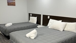Quarto de hotel com duas camas, cada uma com colcha cinza acolchoada e travesseiros brancos, um ventilador de teto e um quadro na parede.
