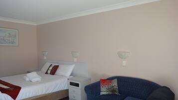 Quarto com cama, mesa de cabeceira, sofá azul e luminária fixada na parede.