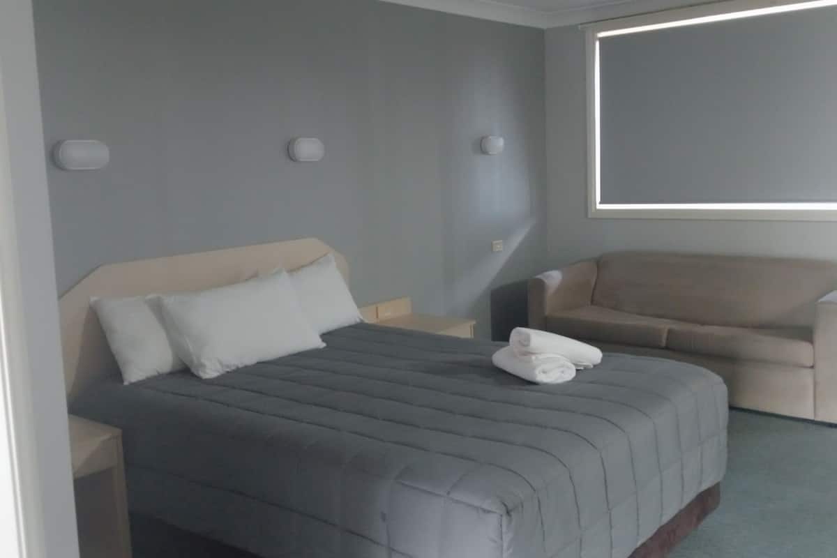 Quarto de hotel com cama, sofá e uma janela grande.