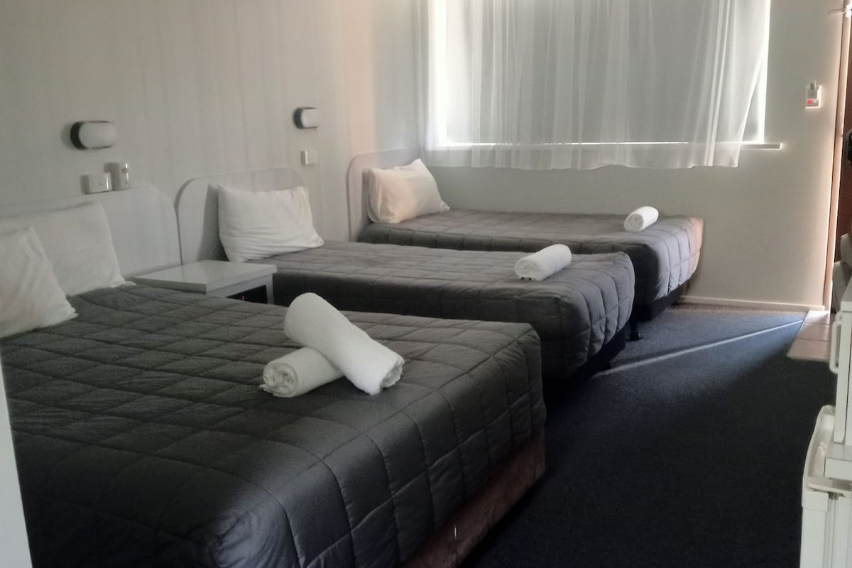 Quarto de hotel com duas camas, um ventilador de teto, uma janela com cortinas e uma mesa de cabeceira com luminária.