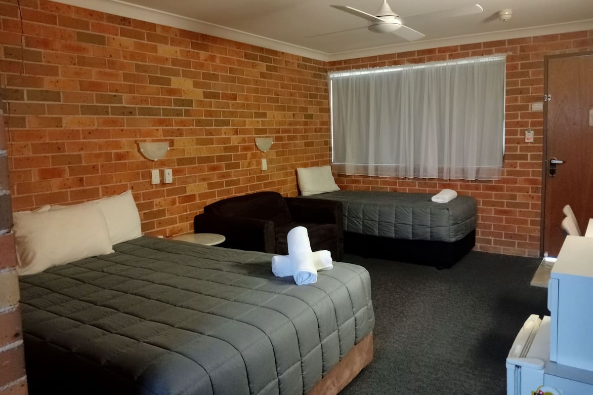 Quarto de hotel com duas camas, parede de tijolos, ventilador de teto e janela com cortinas.