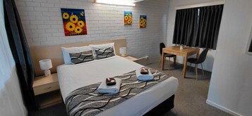 Quarto de hotel com cama, mesas de cabeceira, escrivaninha e cadeiras.