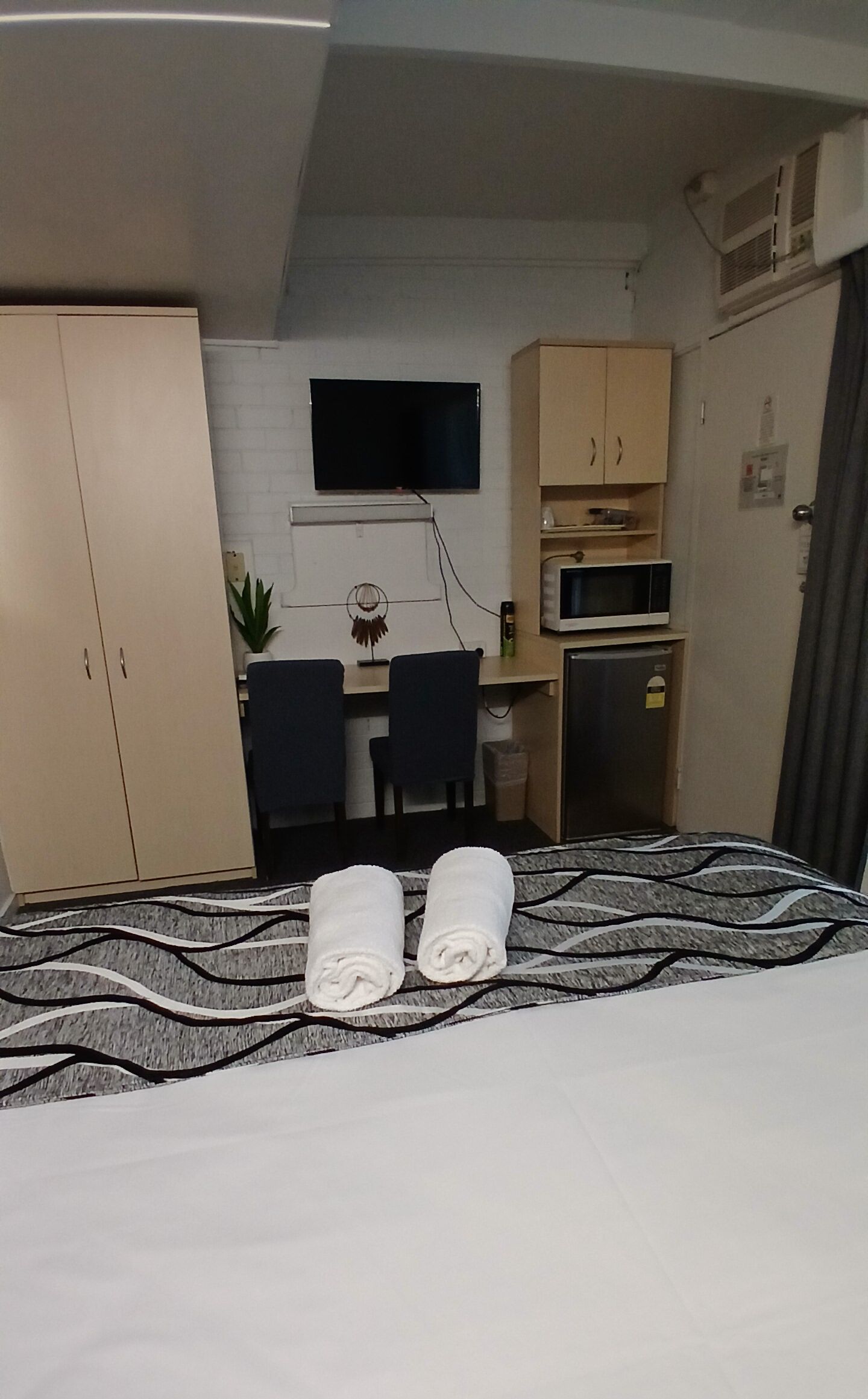 Quarto de hotel com cama, escrivaninha, micro-ondas e televisão.