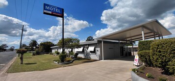 Um motel com área de estacionamento coberta, placa indicando quartos indisponíveis e céu claro.