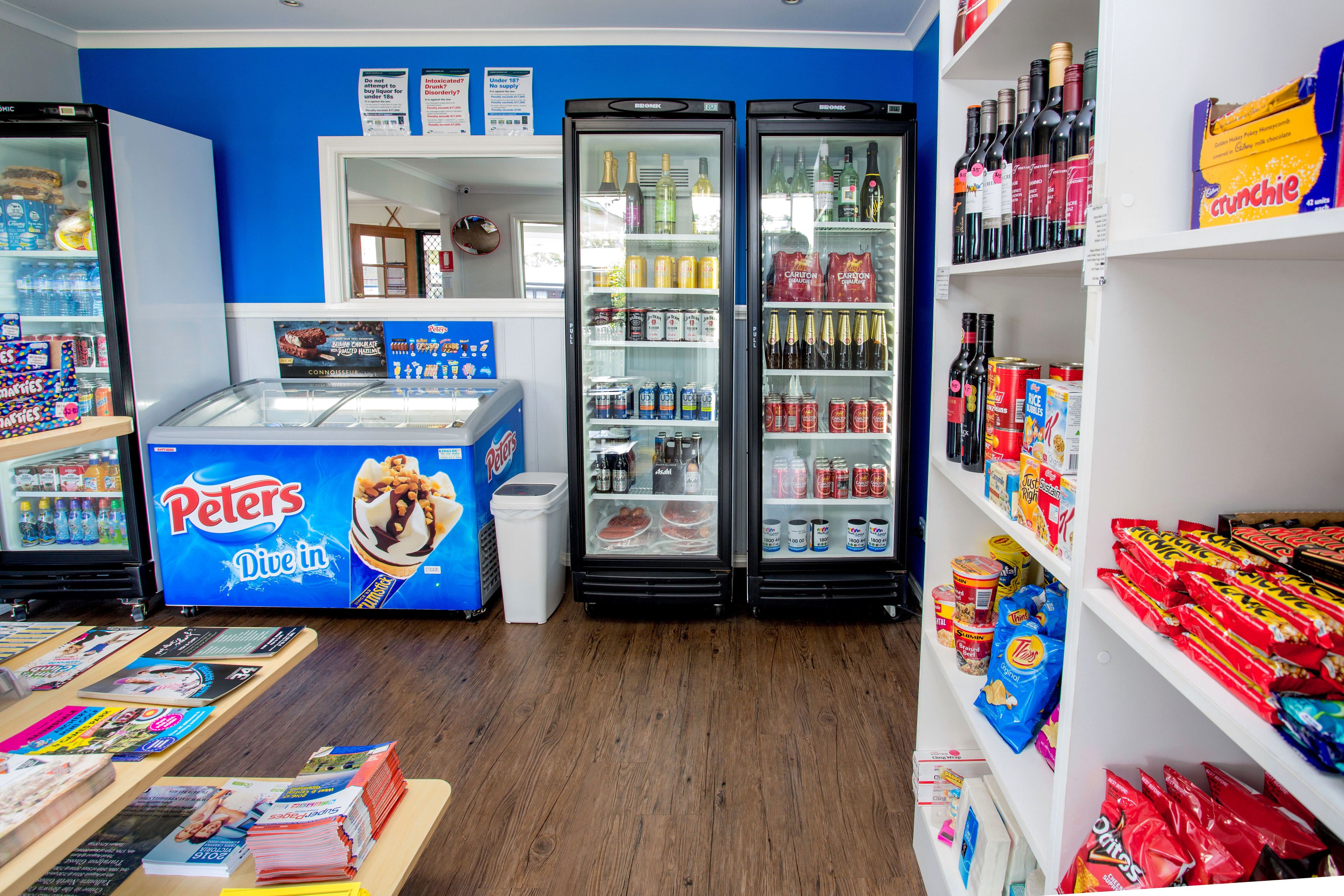 Uma loja de conveniência com seções refrigeradas, prateleiras repletas de lanches e uma exposição de revistas.