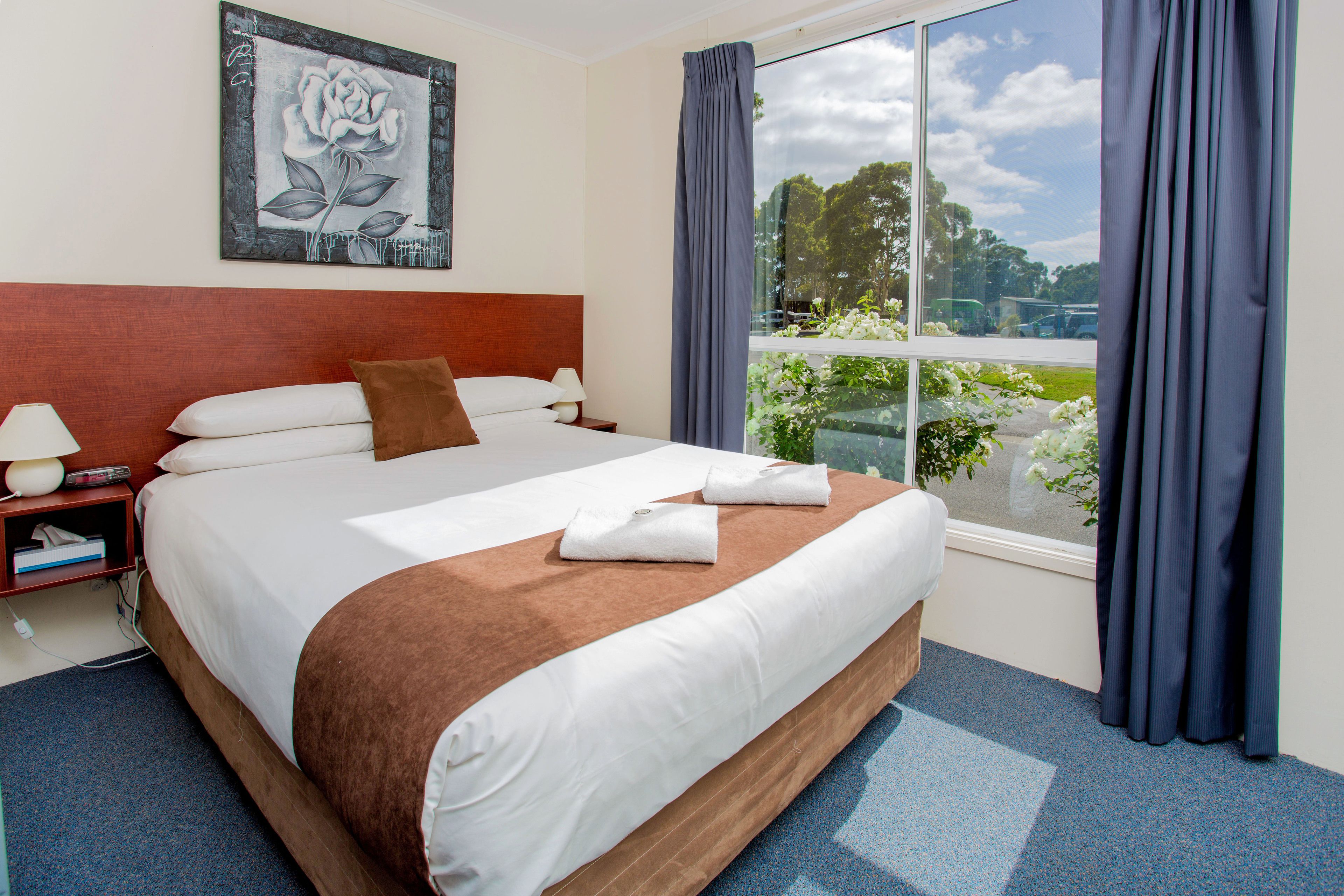 Quarto de hotel com uma cama grande, uma mesa de cabeceira, uma luminária e uma janela com cortinas.