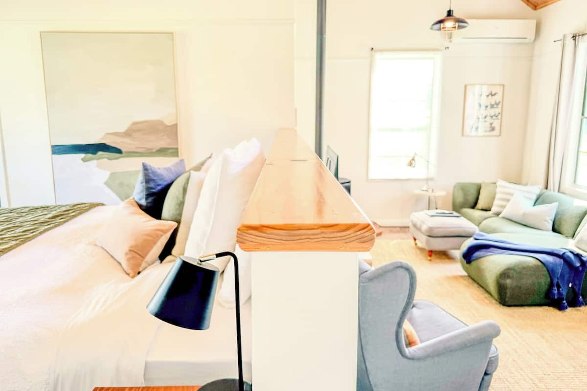 Quarto moderno com cama, luminária de cabeceira e sofá verde.