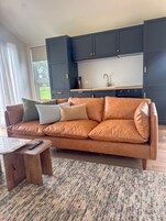 Uma sala de estar moderna com um sofá de couro, uma mesa de centro e uma cozinha ao fundo.