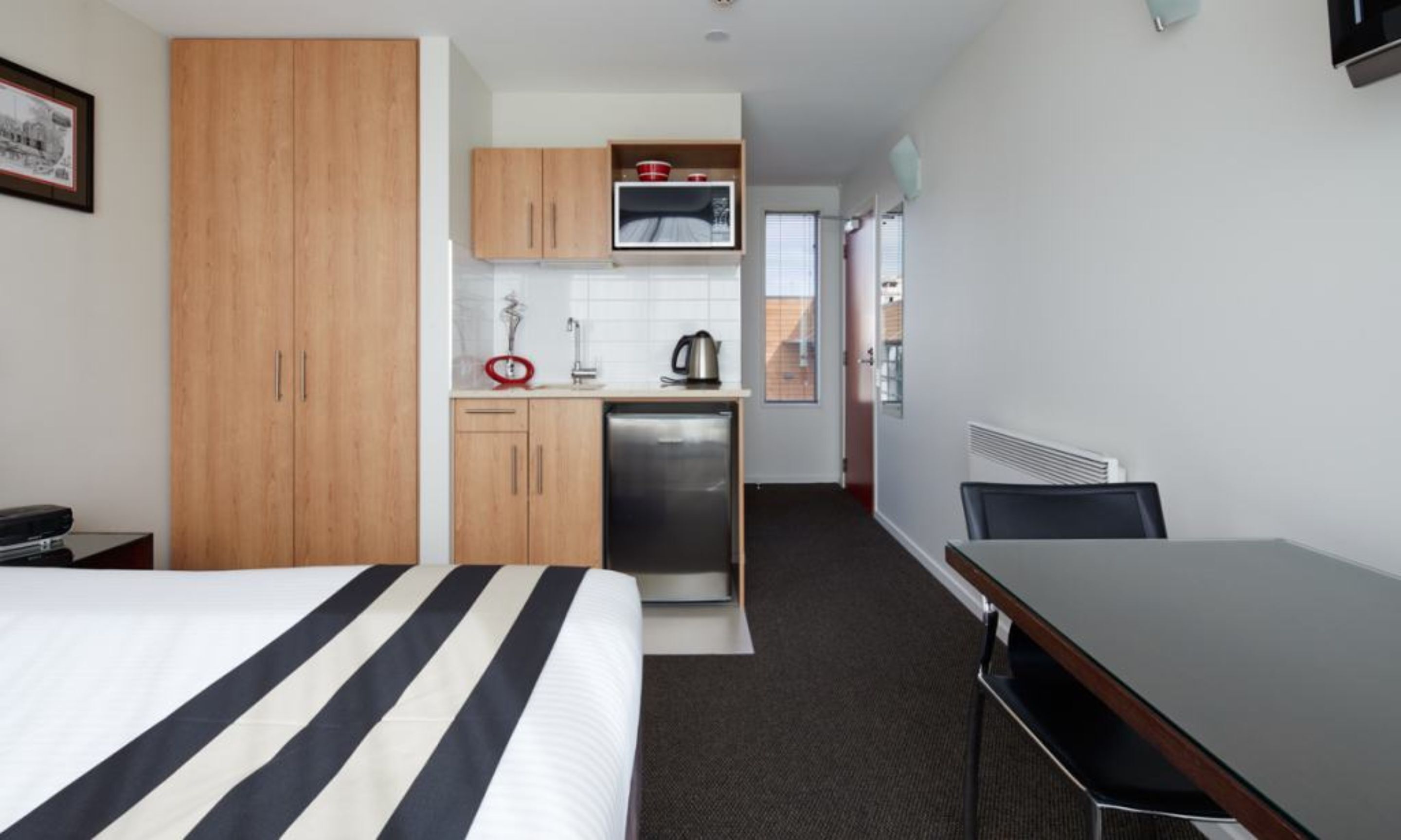 Quarto de hotel compacto com cama, escrivaninha, cozinha compacta e vista para o exterior.