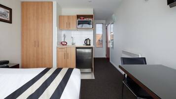 Quarto de hotel compacto com cama, escrivaninha, cozinha compacta e vista para o exterior.