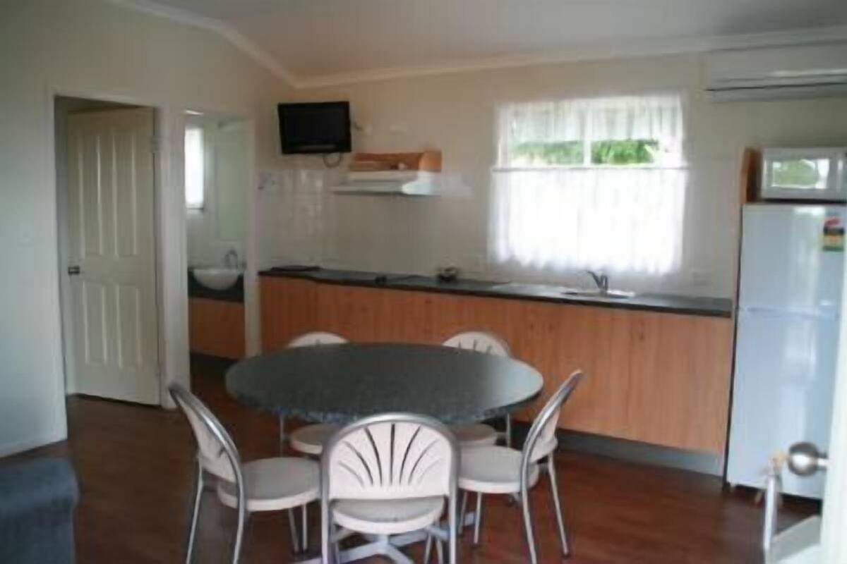 Uma cozinha compacta com uma mesa de jantar e cadeiras, uma televisão acima do balcão e uma geladeira.