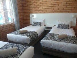 Quarto de hotel com duas camas de solteiro, uma mesa de cabeceira e uma janela com cortinas.