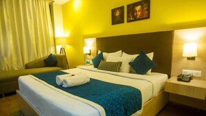 Quarto de hotel com uma cama grande, um sofá, uma mesa de cabeceira com telefone e duas luminárias de parede.