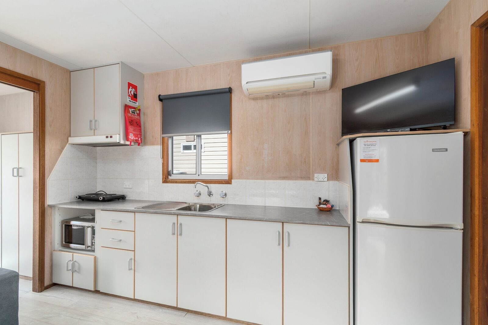 Cozinha compacta com armários brancos, micro-ondas embutido, pia e geladeira.