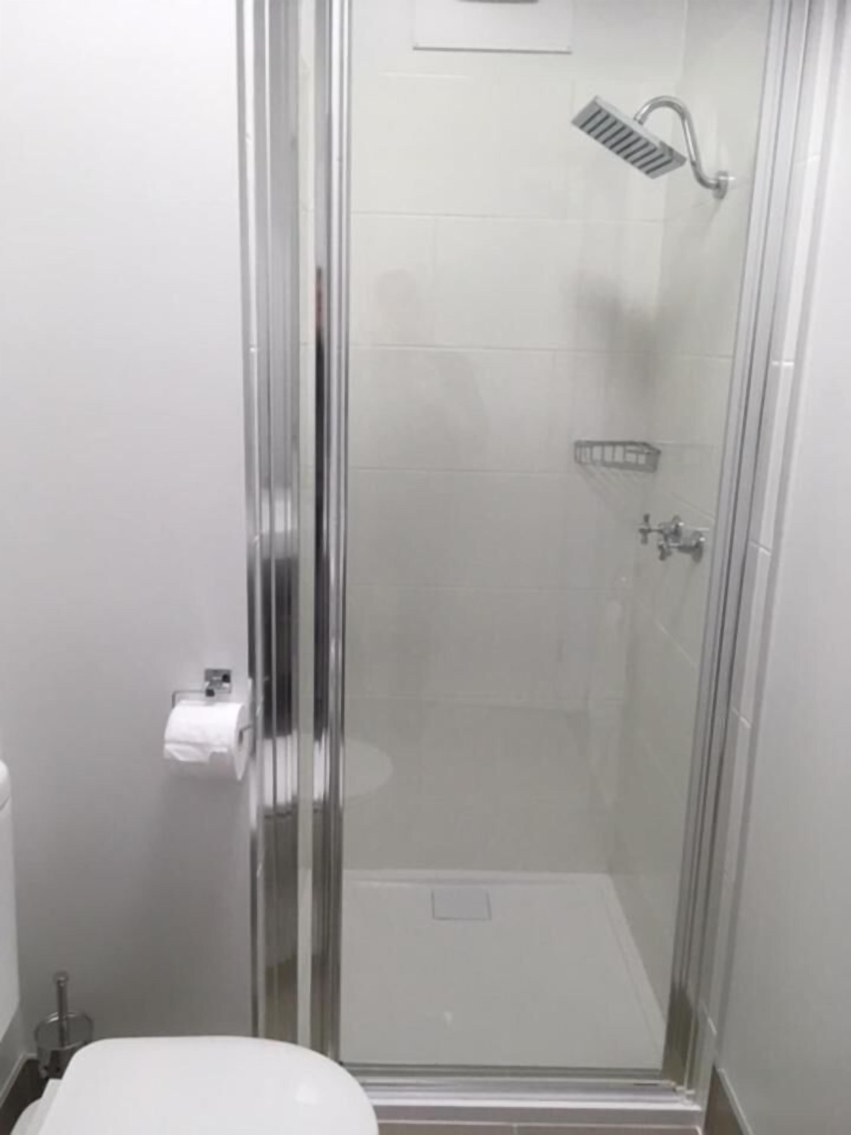 Um chuveiro envidraçado com um chuveiro manual e uma torneira fixa na parede.