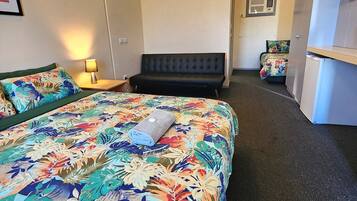 Quarto de hotel com cama, um banco, escrivaninha e televisão.