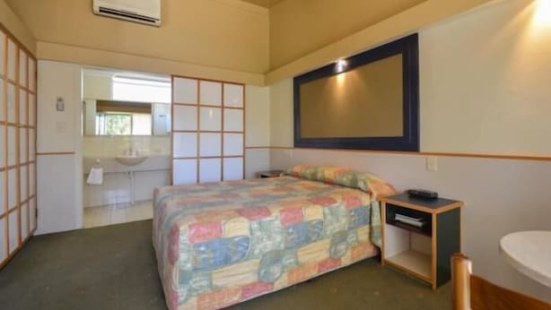Quarto com cama, mesa de cabeceira e espelho na parede.