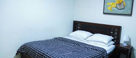 Uma cama de solteiro com cabeceira de madeira, mesa de cabeceira com abajur e um quadro na parede.