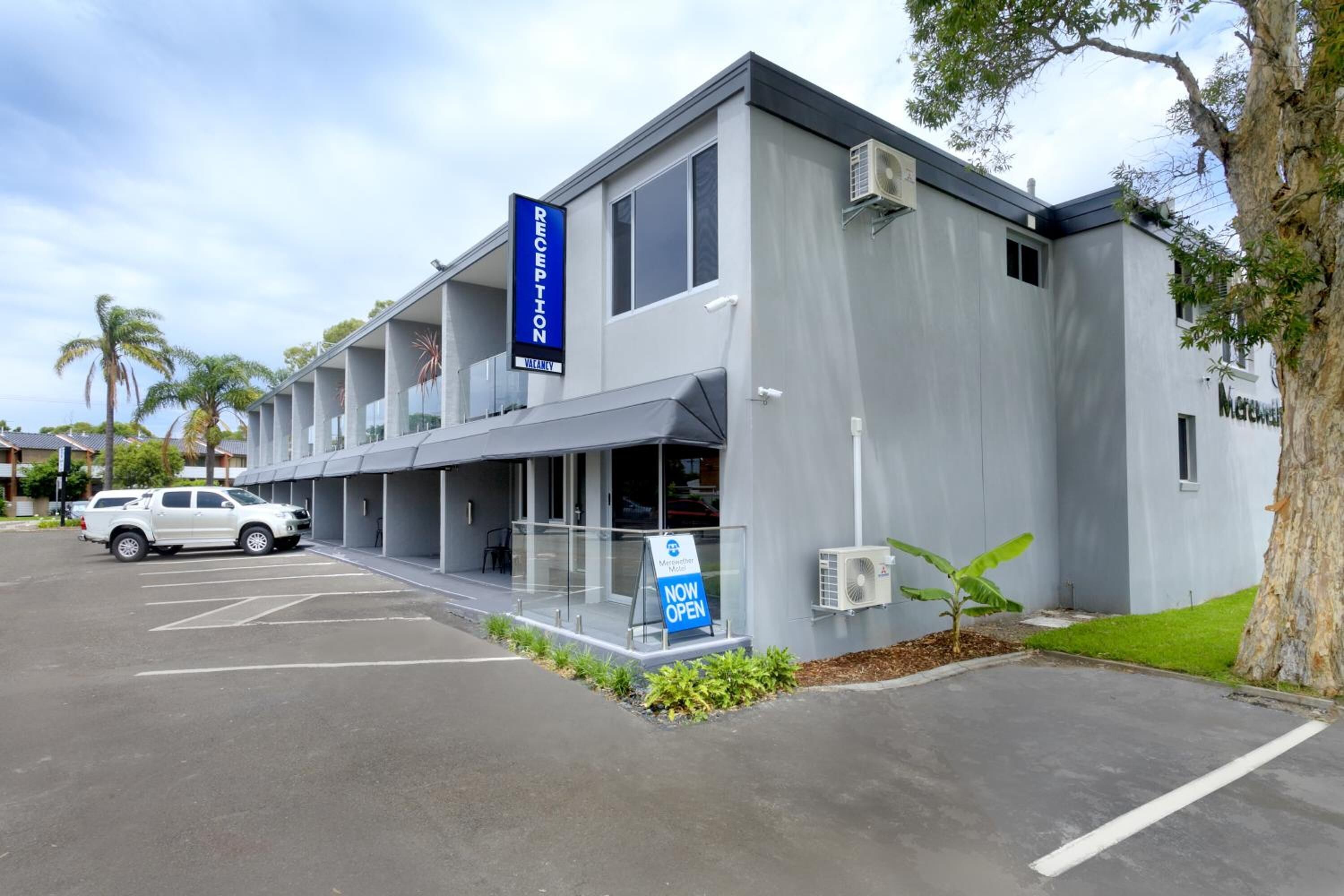 Um hotel moderno com área de recepção, estacionamento e placa indicando que está aberto.