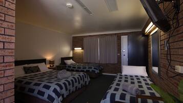 Quarto de hotel com duas camas, parede de tijolos, janela com cortinas, espelho e um respiradouro no teto.