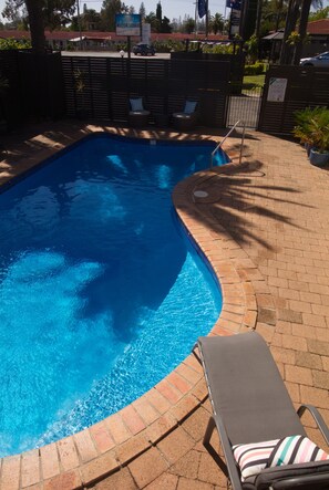 Piscina com borda de tijolos, uma espreguiçadeira e um portão.