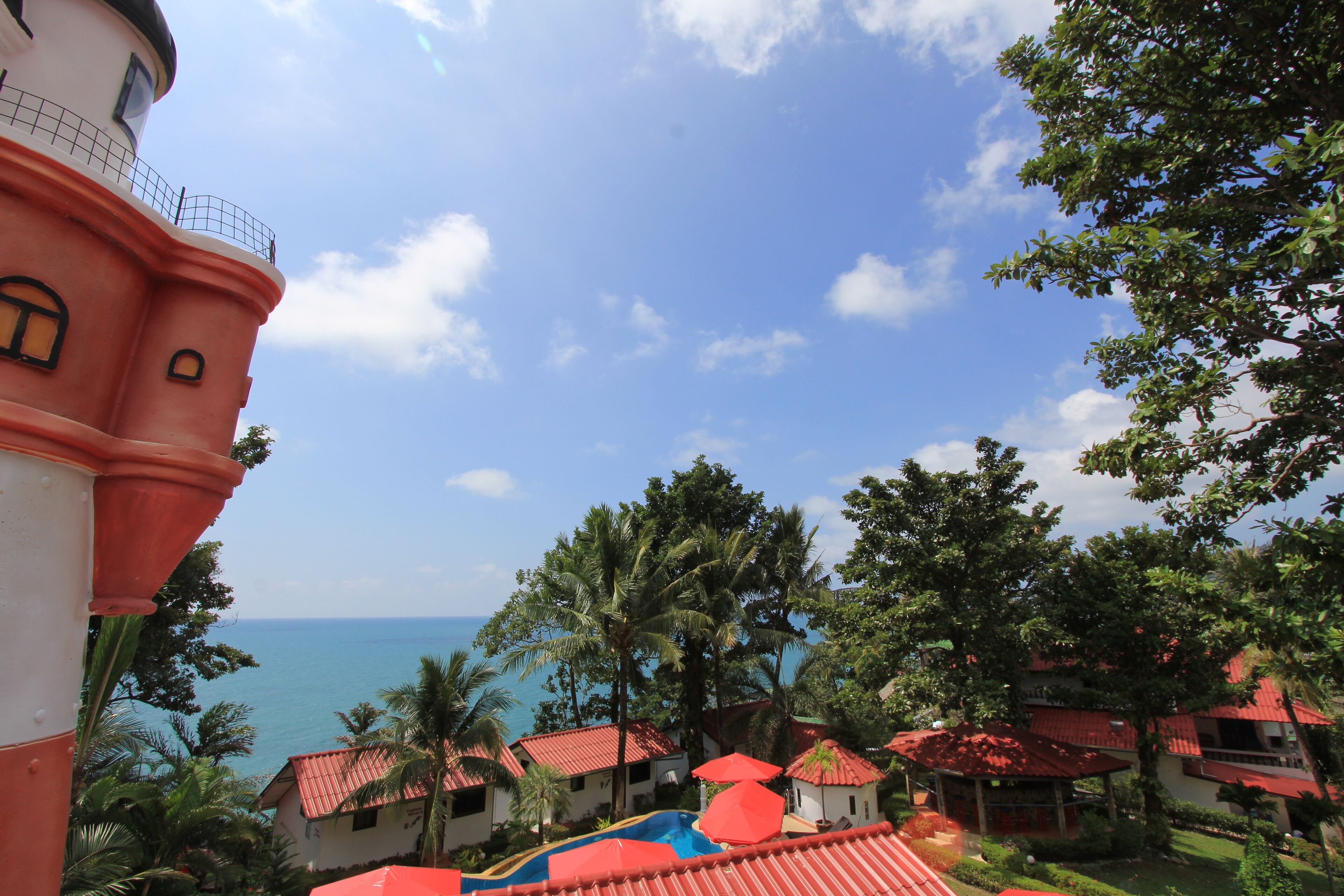 Um resort costeiro com um farol, edifícios com telhados vermelhos e palmeiras.