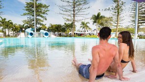 Piscina com dois toboáguas, cercada por palmeiras e um edifício ao fundo.