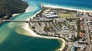 Vista aérea de uma área costeira com praia, marina e área residencial com casas e carros estacionados.