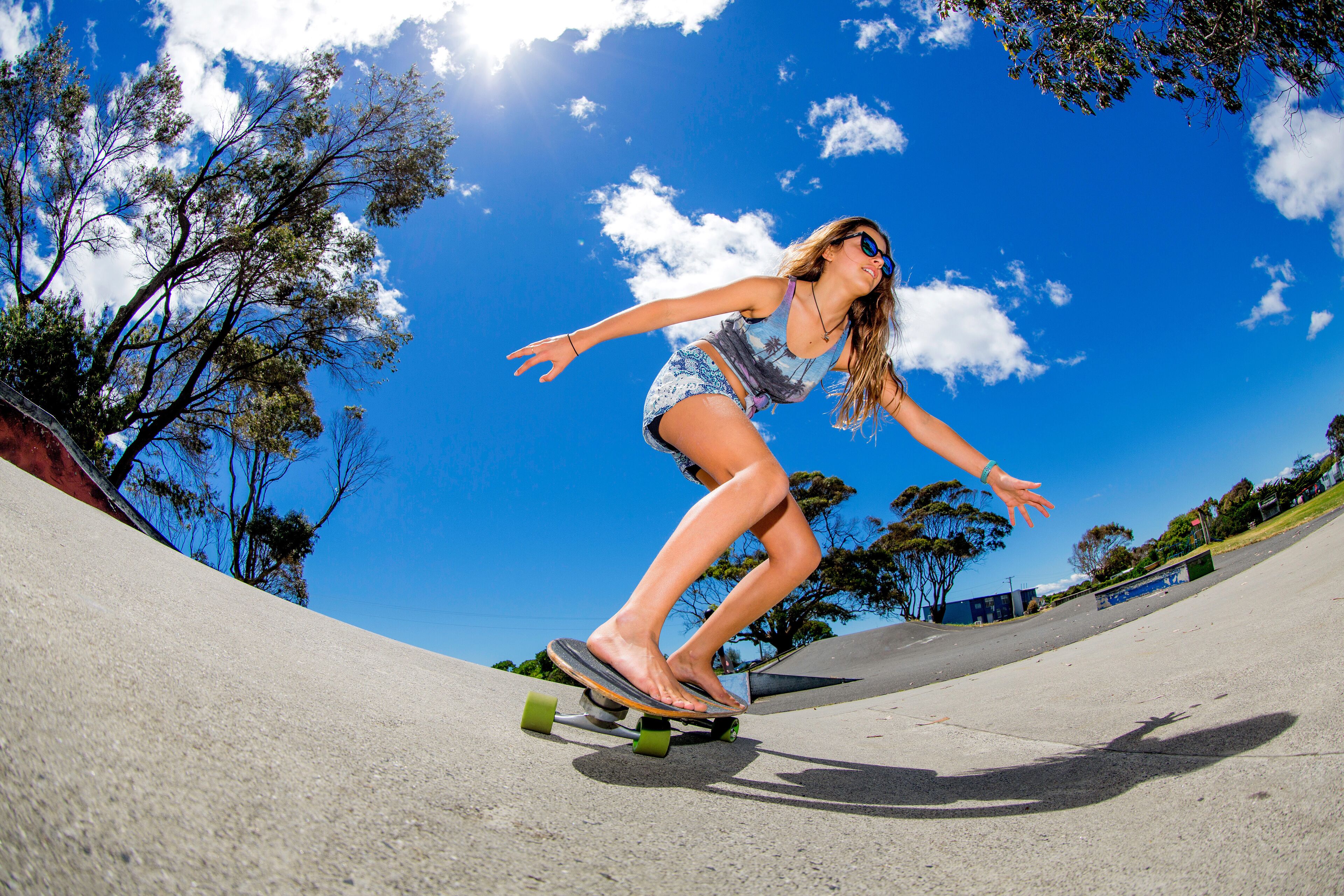 Uma pessoa andando de skate em uma superfície de concreto, com árvores e um céu limpo ao fundo.