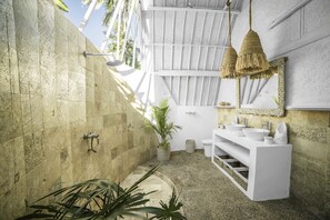Casa de banho com parede de pedra, toucador branco, candeeiro pendente e planta em vaso.