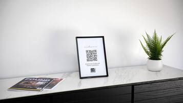 Placa de boas-vindas emoldurada com um código QR num balcão de mármore branco, uma revista intitulada "FOUND" e uma planta em vaso.