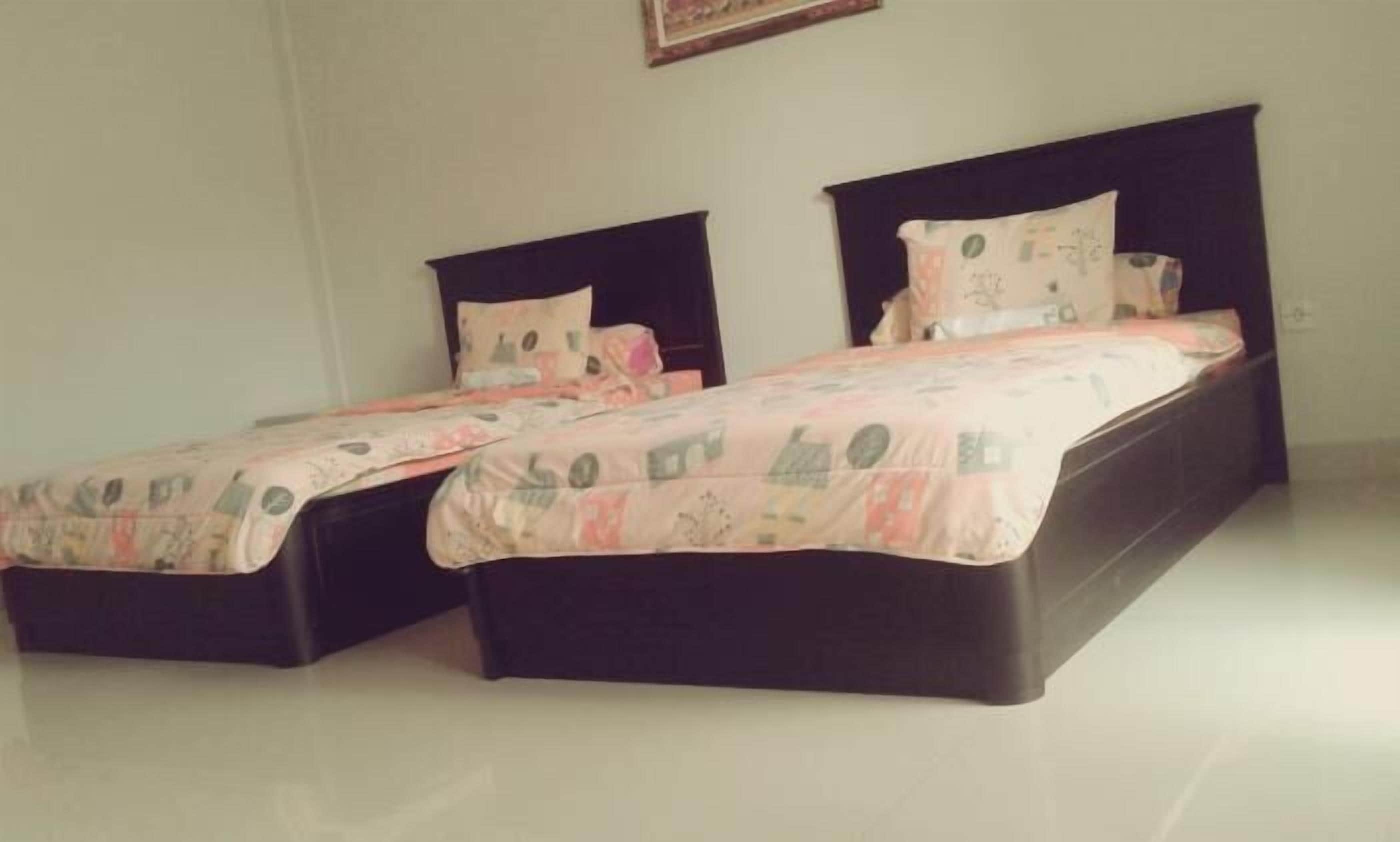 Uma cama de casal com cabeceira escura e colcha florida.