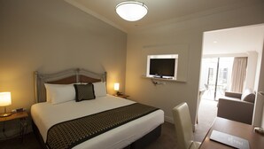 Quarto de hotel com uma cama grande, televisão fixada na parede, secretária com um computador portátil e uma cadeira.