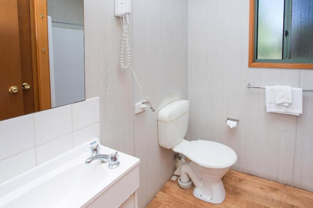 Uma casa de banho pequena com sanita branca, lavatório branco e chuveiro.