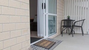Fachada de tijolos com porta de vidro deslizante que dá para uma varanda. Há uma pequena mesa, uma cadeira e um vaso de planta na varanda.