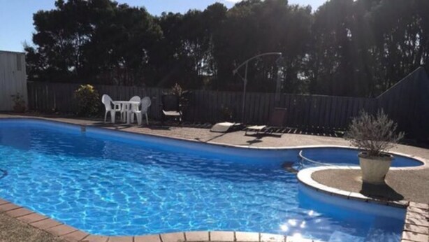 Piscina com borda curva, rodeada por uma barreira de pedras. Há espreguiçadeiras e uma mesa pequena perto da piscina.