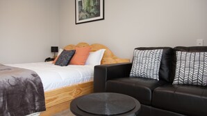 Quarto com uma cama, um sofá de couro preto, uma mesa redonda pequena e um quadro na parede.