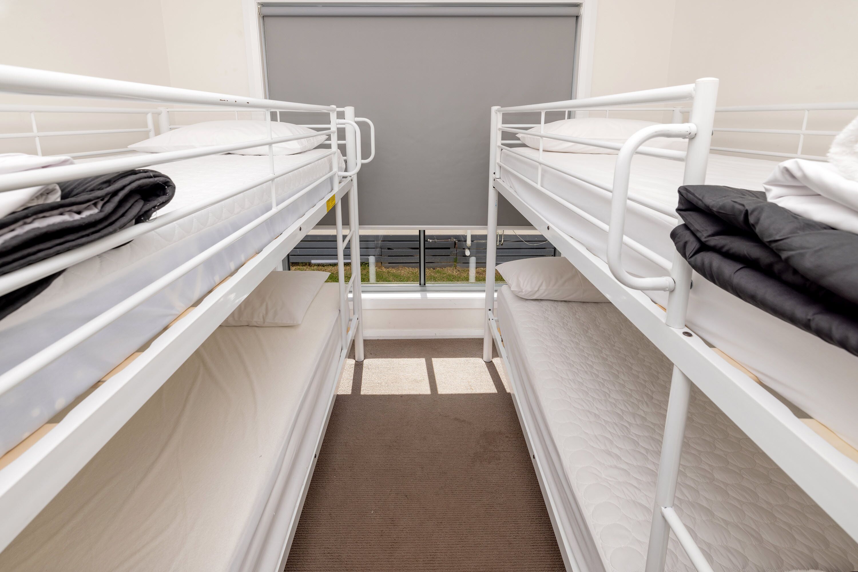 Quarto com beliche, janela e vista para uma área gramada.