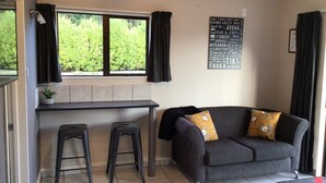 Uma sala de estar moderna com um sofá cinza escuro, dois banquinhos pretos, uma mesa pequena e uma janela com cortinas.