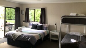 Quarto com cama, beliche, mesa de cabeceira, abajur e janela com cortinas.