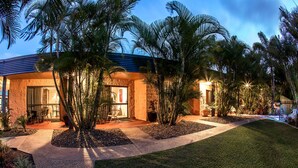 Uma casa moderna com um pátio, palmeiras e um gramado bem cuidado.