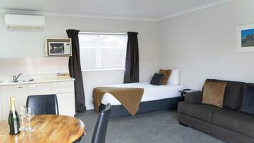 Quarto de hotel com cama, sofá, mesa de jantar com cadeiras, micro-ondas, pia e janela com cortinas.
